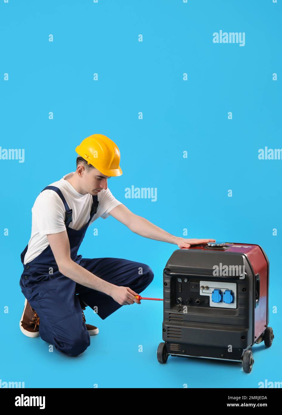 Male worker repairing portable gasoline generator on blue background ...