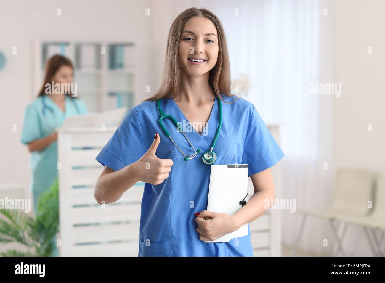 Female medical assistant with folder showing thumb-up in clinic Stock ...