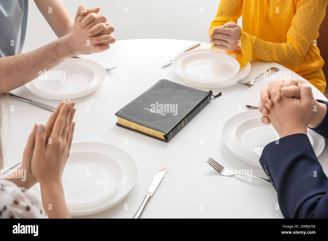 Group of people praying with Holy Bible before dinner in room, closeup ...