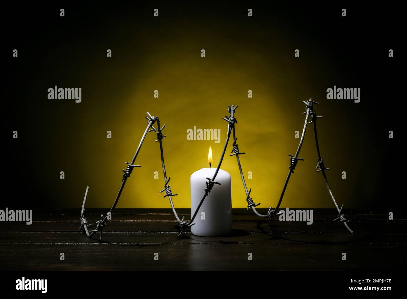 Burning candle and barbed wire on table against dark background ...