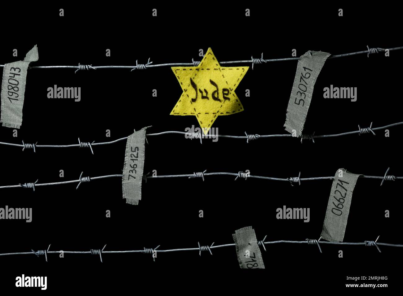Barbed wire with Jewish badge and prisoner numbers on dark background ...