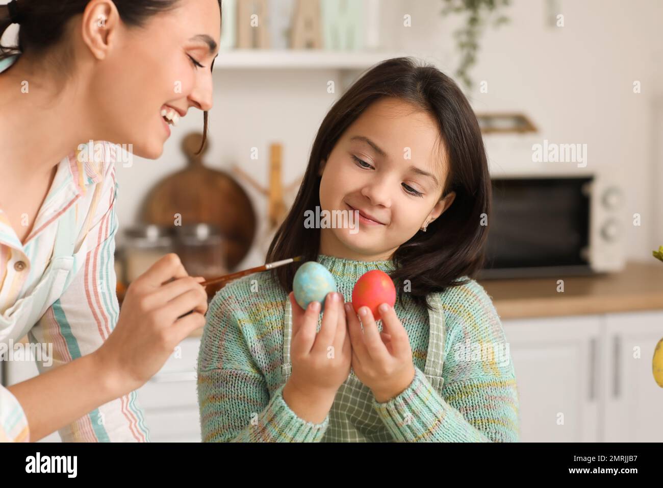 Little girl with Easter eggs and her mother in kitchen, closeup Stock ...