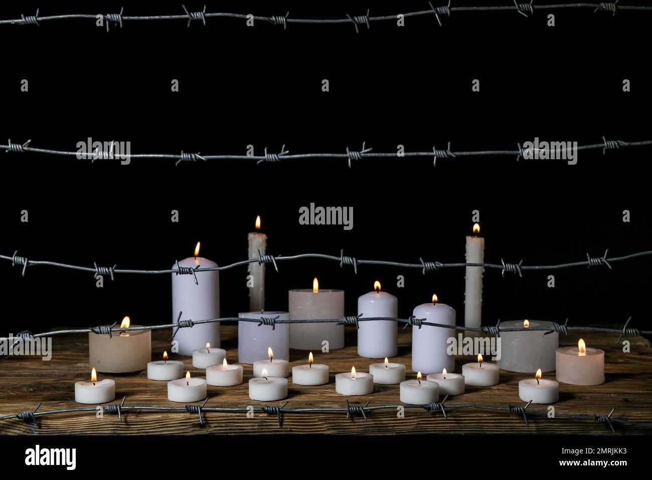 Barbed wire and burning candles on table against dark background ...