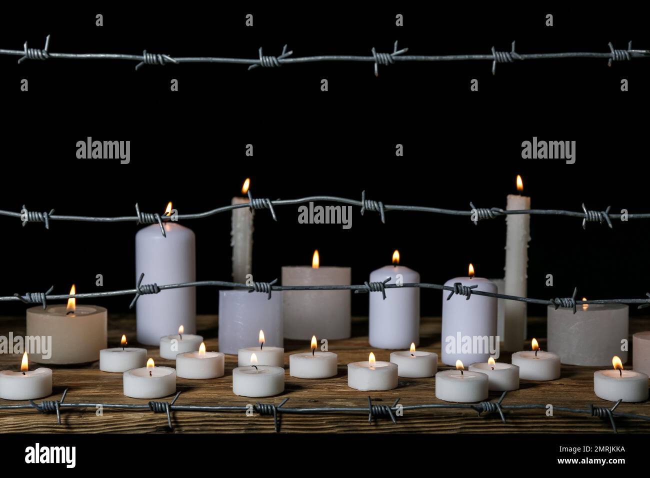 Barbed wire and burning candles on table against dark background ...