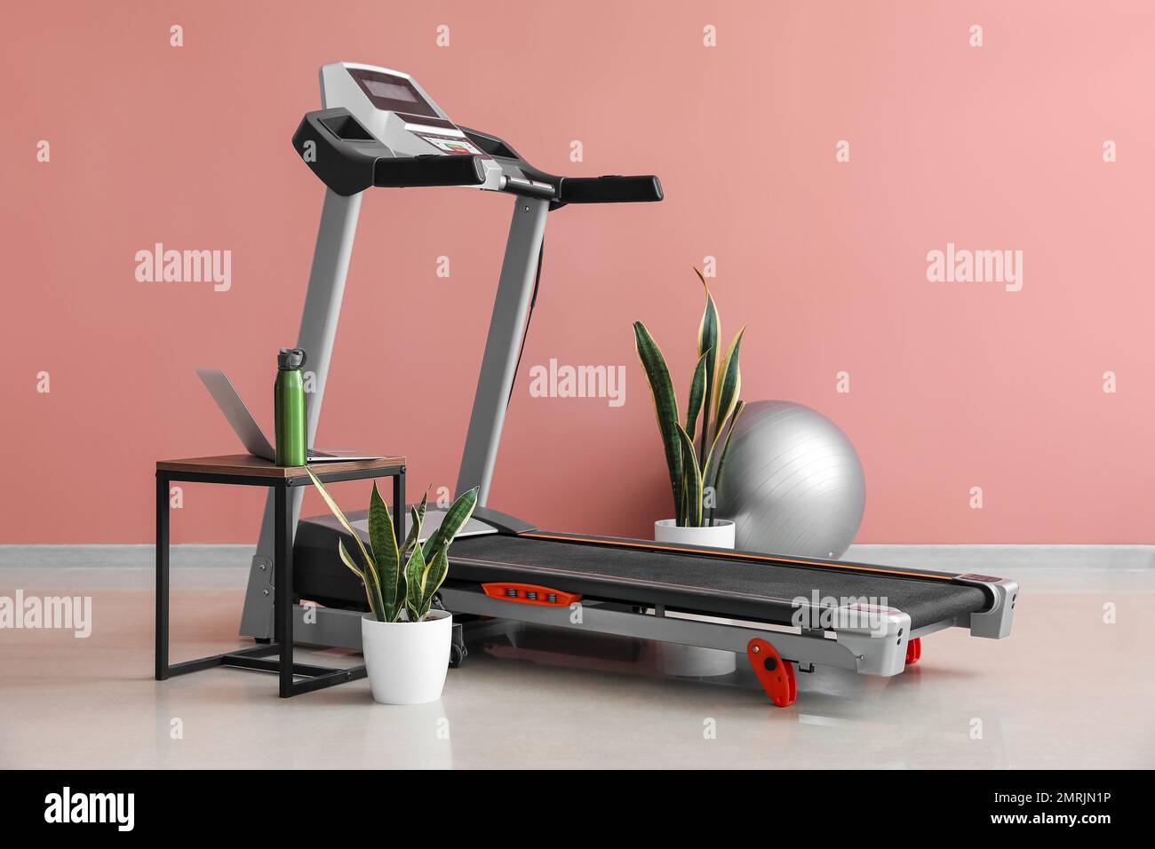Interior of room with modern treadmill and laptop on table near pink ...