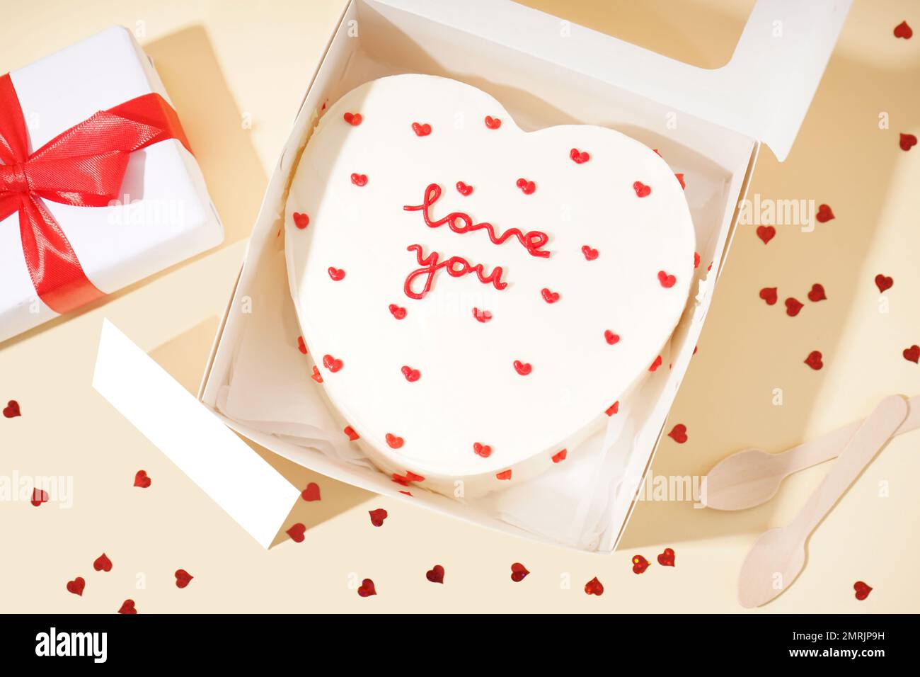 Opened box with heart-shaped bento cake and gift on beige background ...