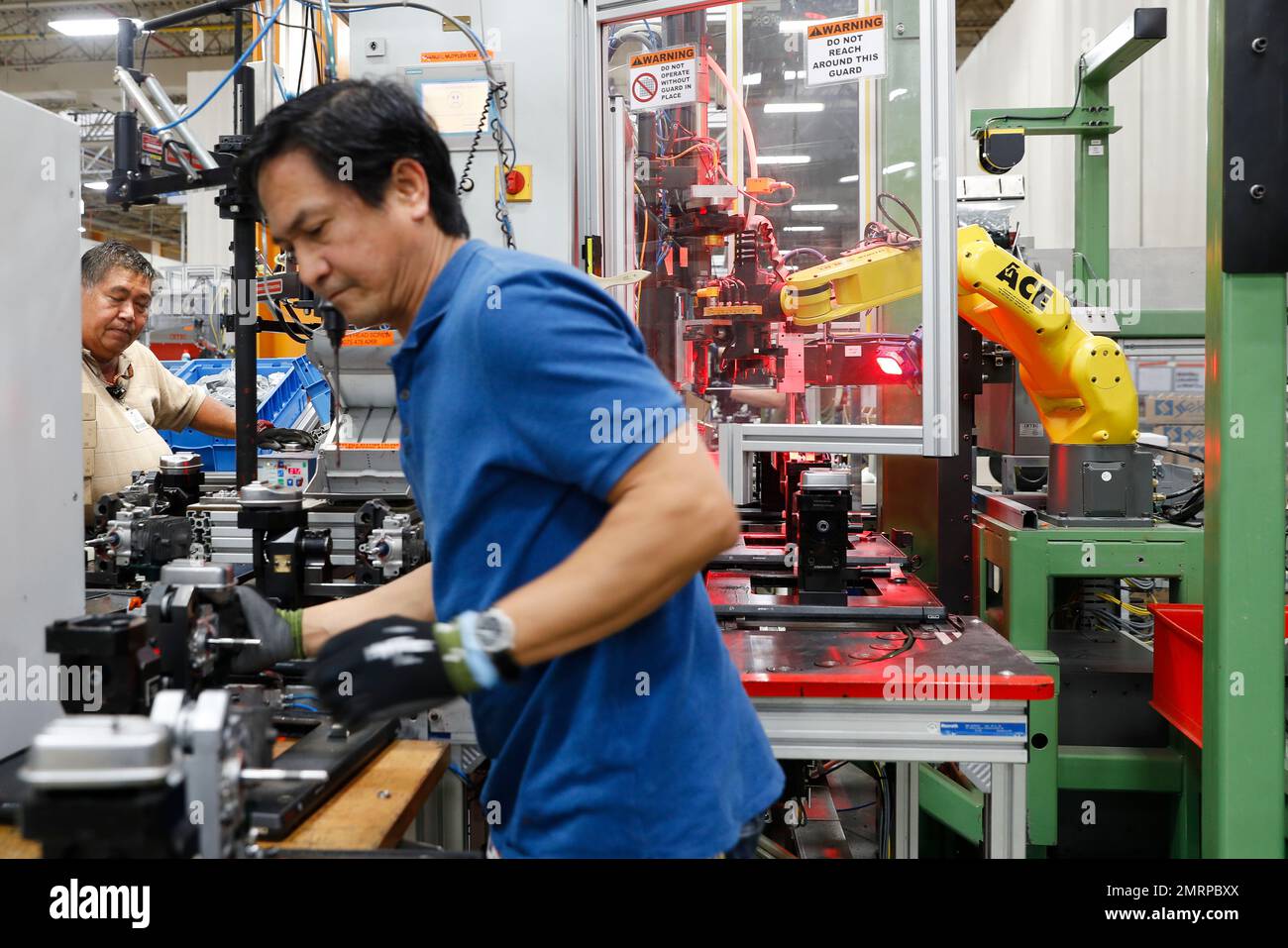 A collaborative robot, right, works alongside manufacturing laborers on ...
