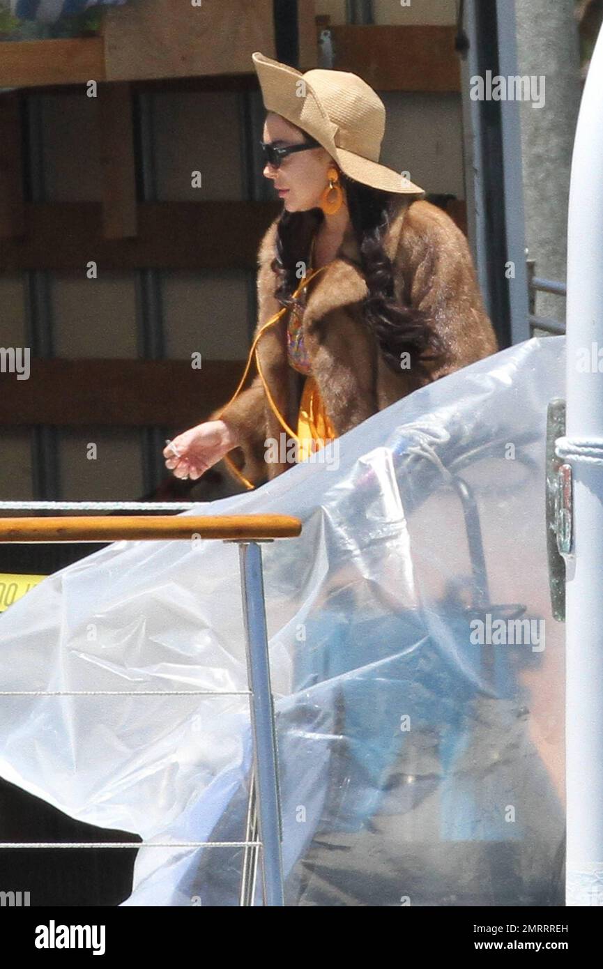 Smoking a cigarette, Lindsay Lohan portrays Elizabeth Taylor, wearing a ...