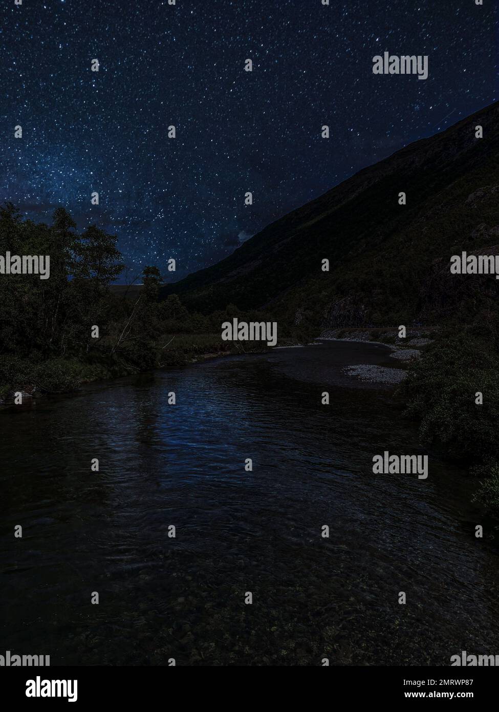 A vertical shot a river and a mountainside under the blue starry sky at ...