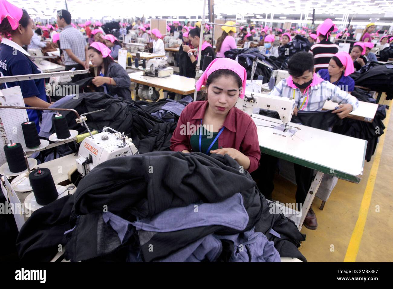 Cambodian garment workers sew clothes in a factory as they wait for ...