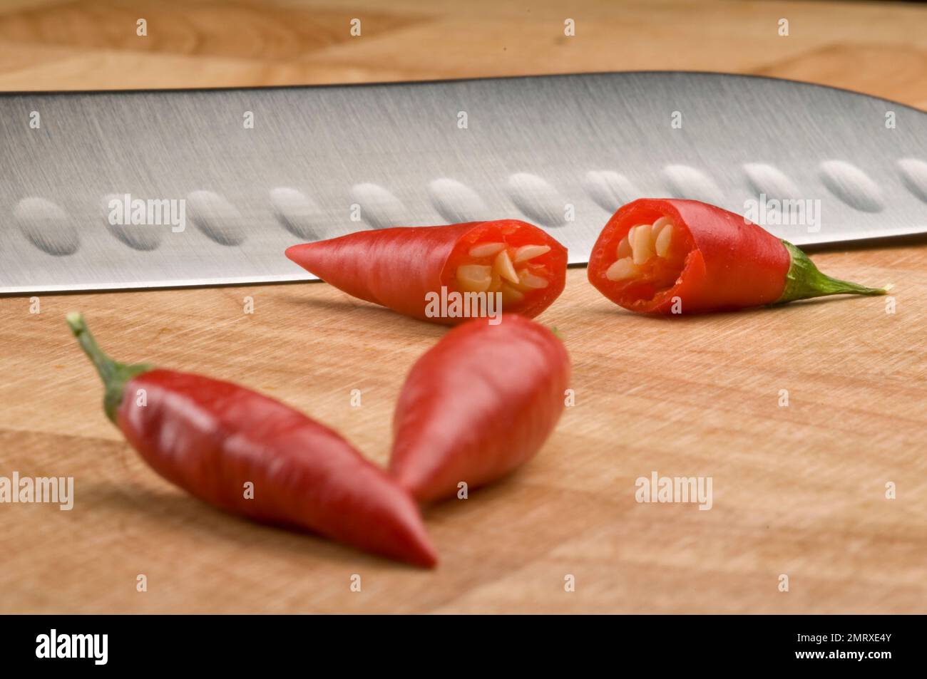 Four red chilli peppers one cut in half on a chopping board with a ...