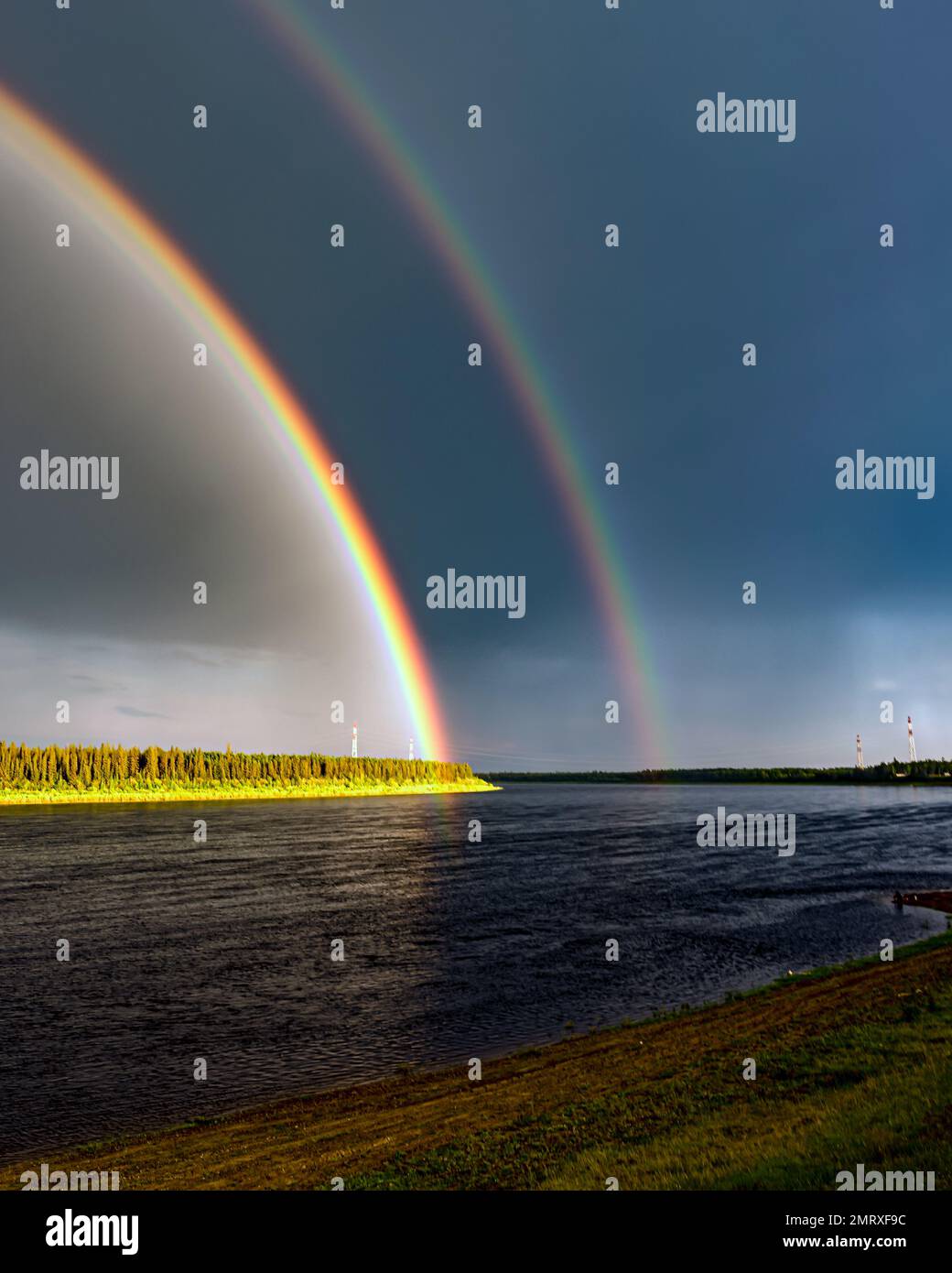 A double rainbow against a backdrop of bright blue clouds emerges from ...