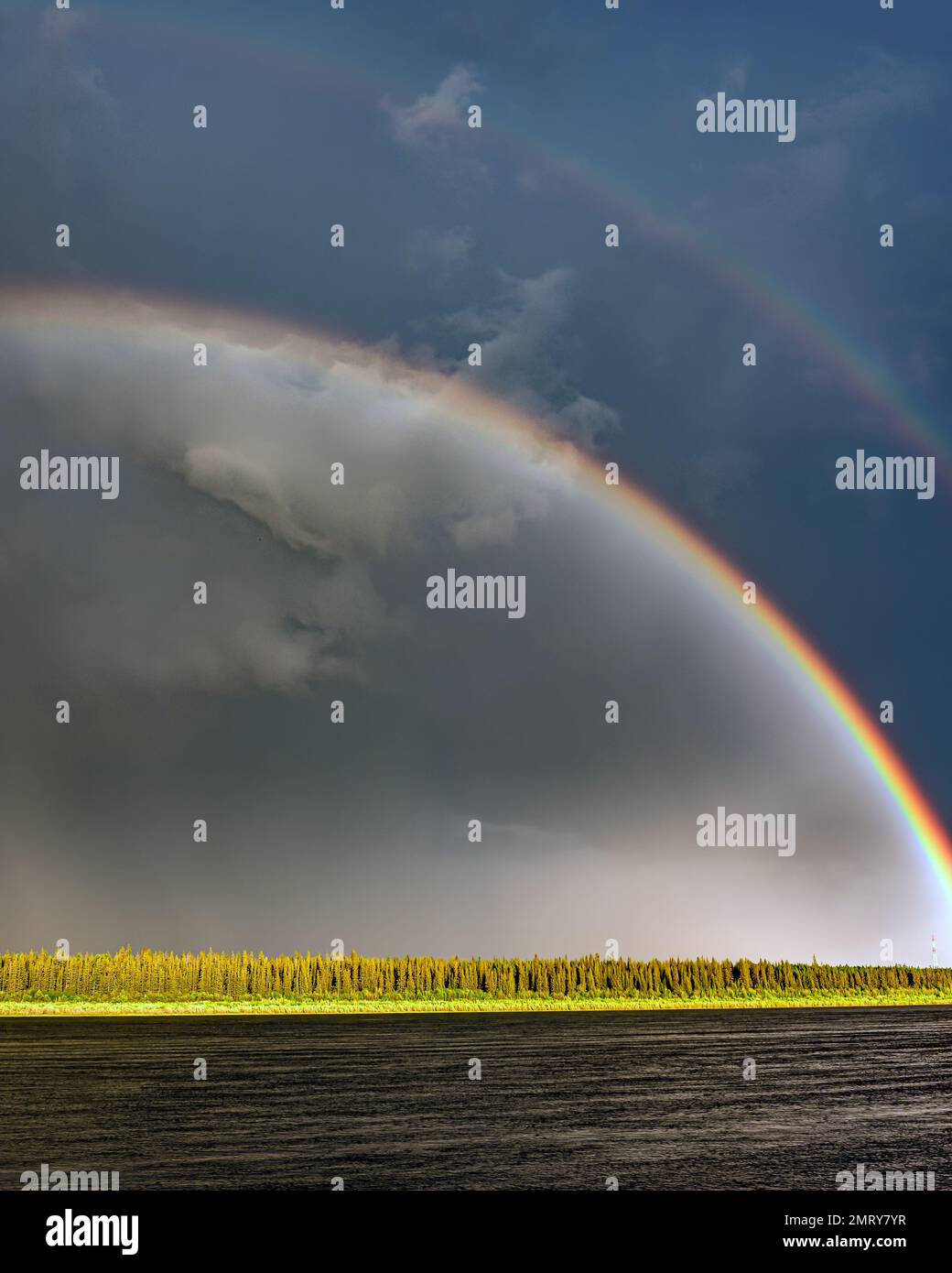 A double rainbow over a river after rain against a dark sky with white ...