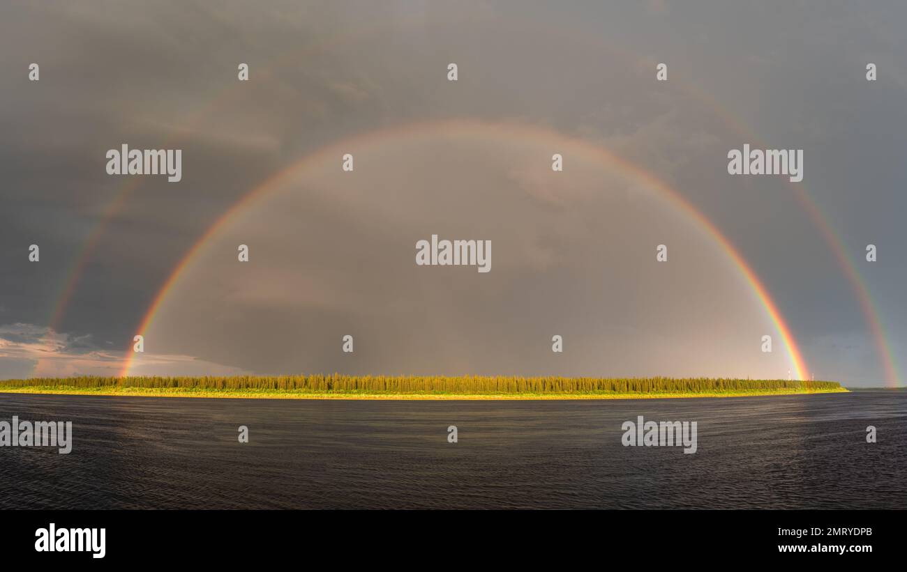 Panorama of a full double rainbow against a blue sky and white clouds ...