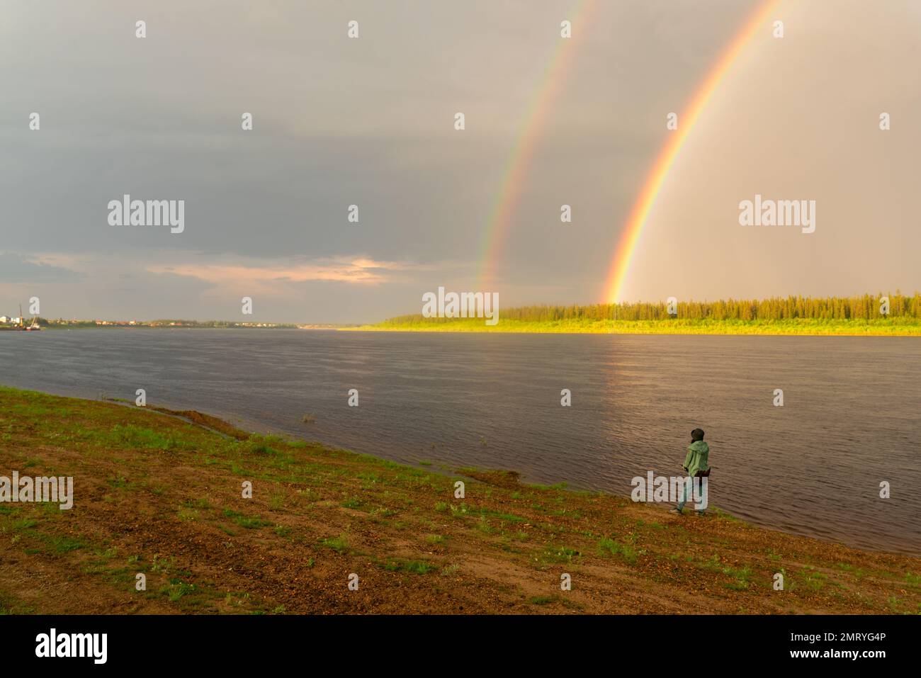 A girl fishes on the bank of a river with a double rainbow in the ...