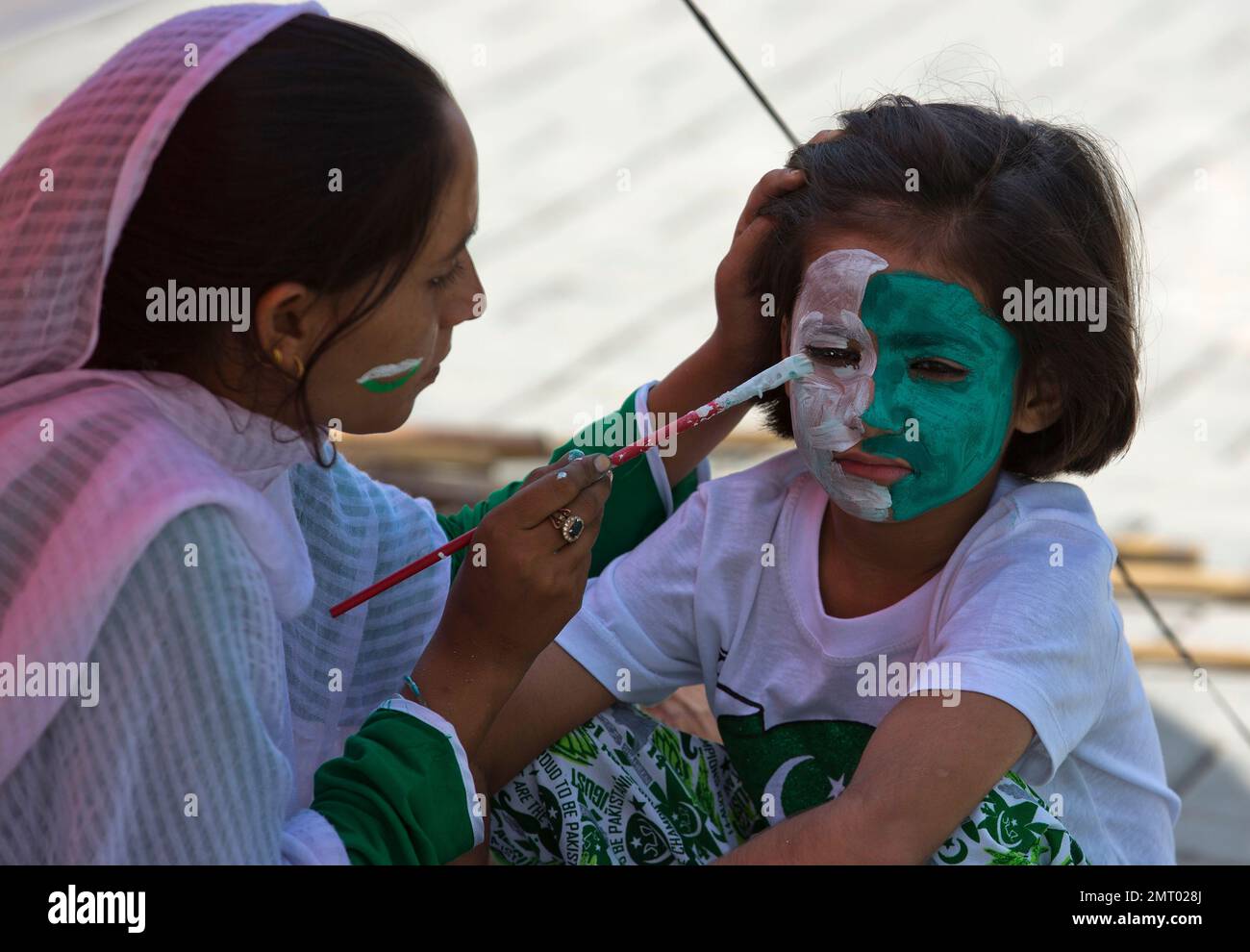 A Pakistani vendor paints the color of the Pakistani flag on a girl's ...