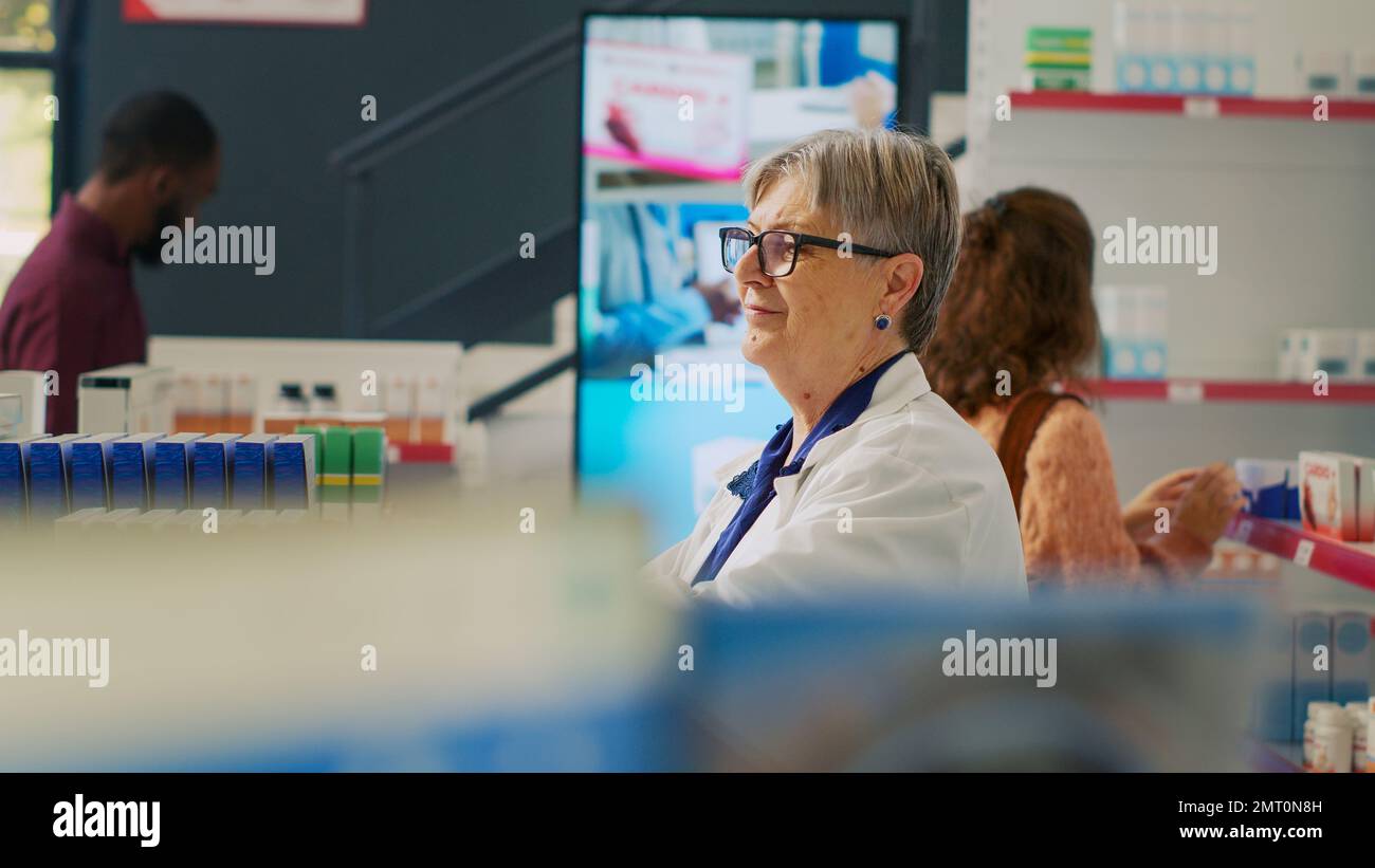 Senior health specialist looking at vitamins boxes on pharmacy shelves ...