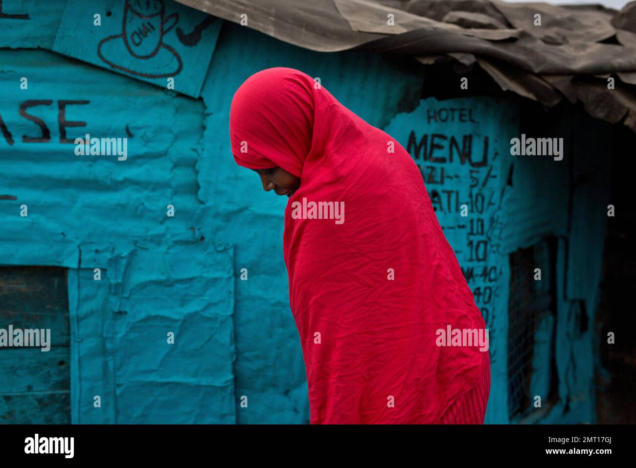 A Kenyan woman stands by a closed restaurant, fixing her veil, in ...