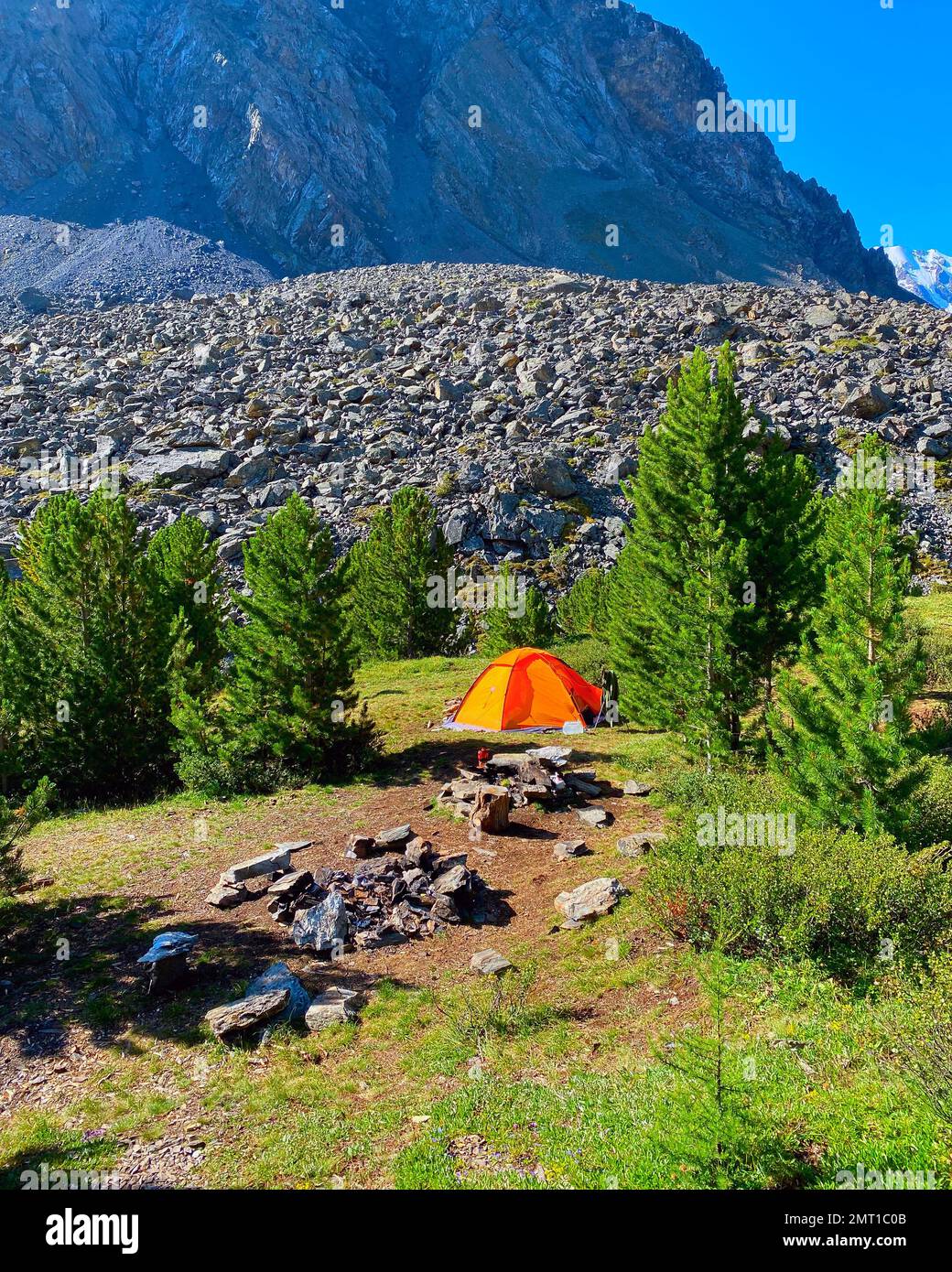 An orange tourist tent stands at the end of a trail under a stone cliff ...