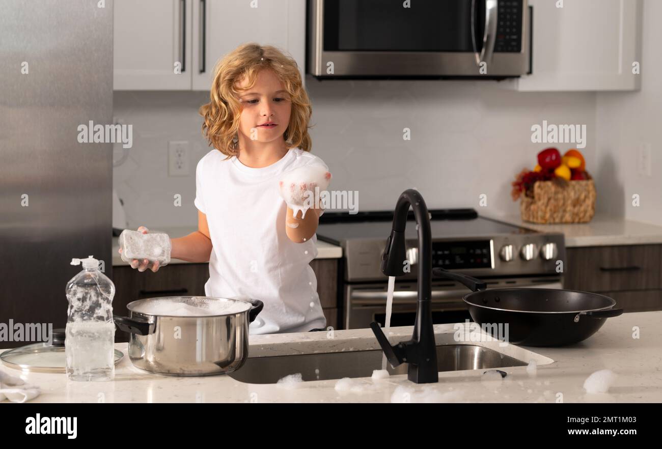 Child boy washing dishes in the kitchen interior. Dishwashing liquid ...