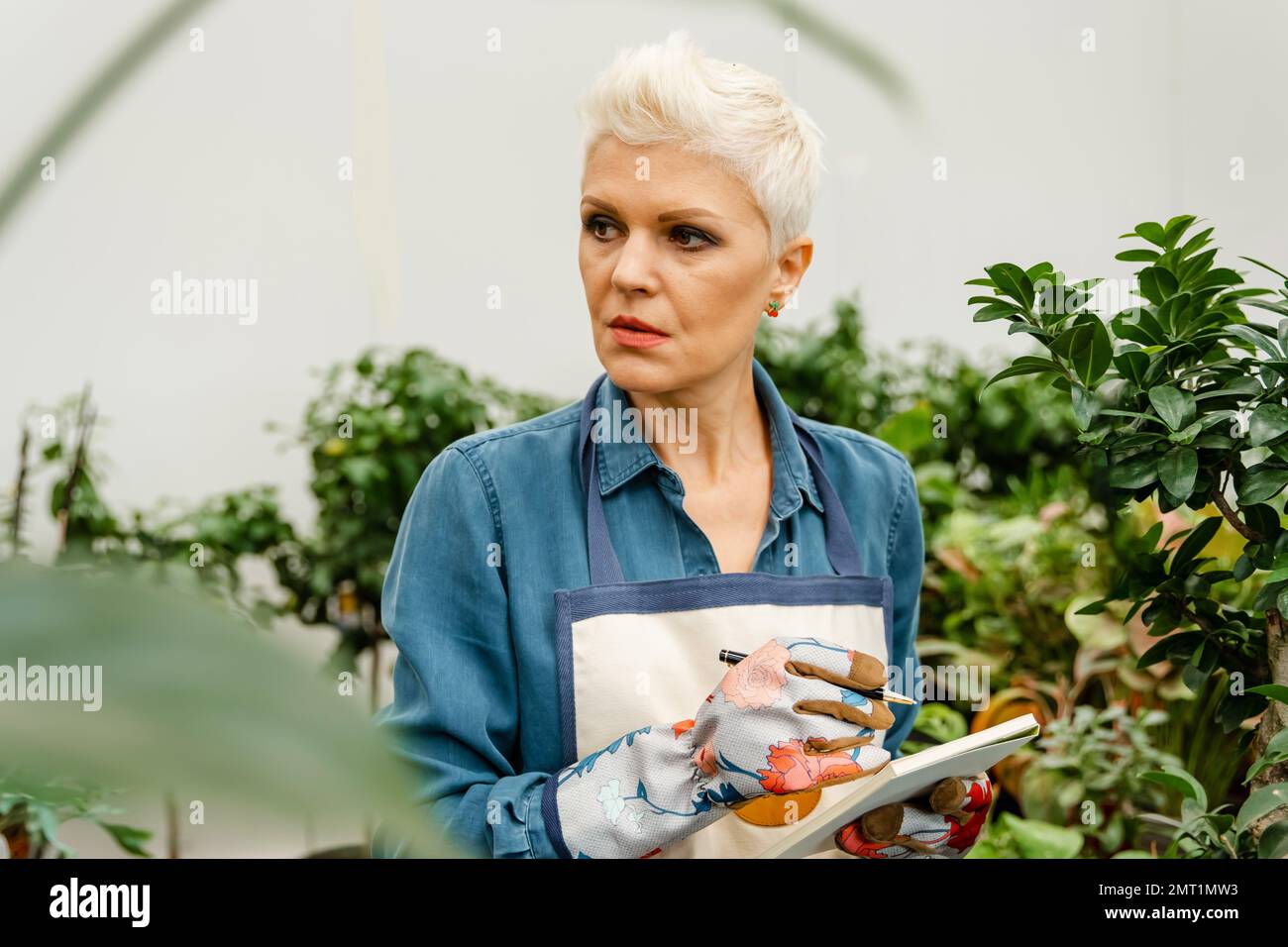 Serious woman gardener checking plants, taking notes about greenery ...
