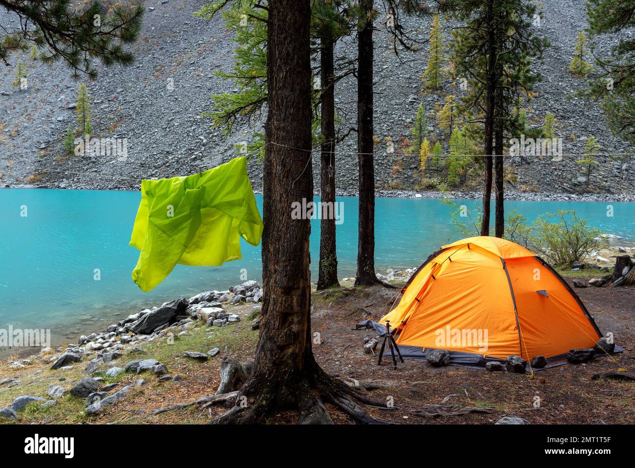 An orange tent stands in spruce trees on the shore of the high-altitude ...