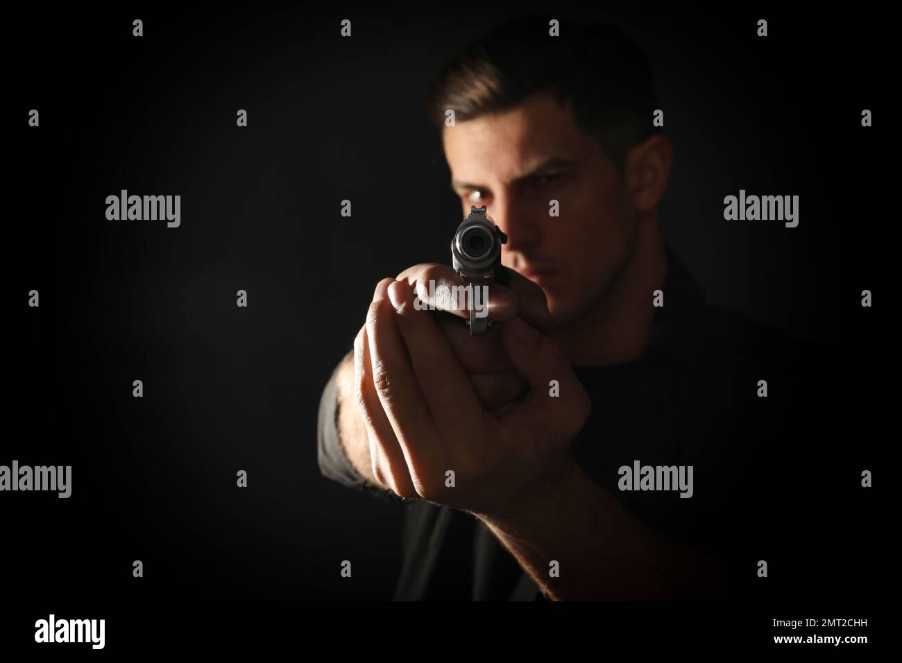 Professional killer with gun on black background Stock Photo - Alamy