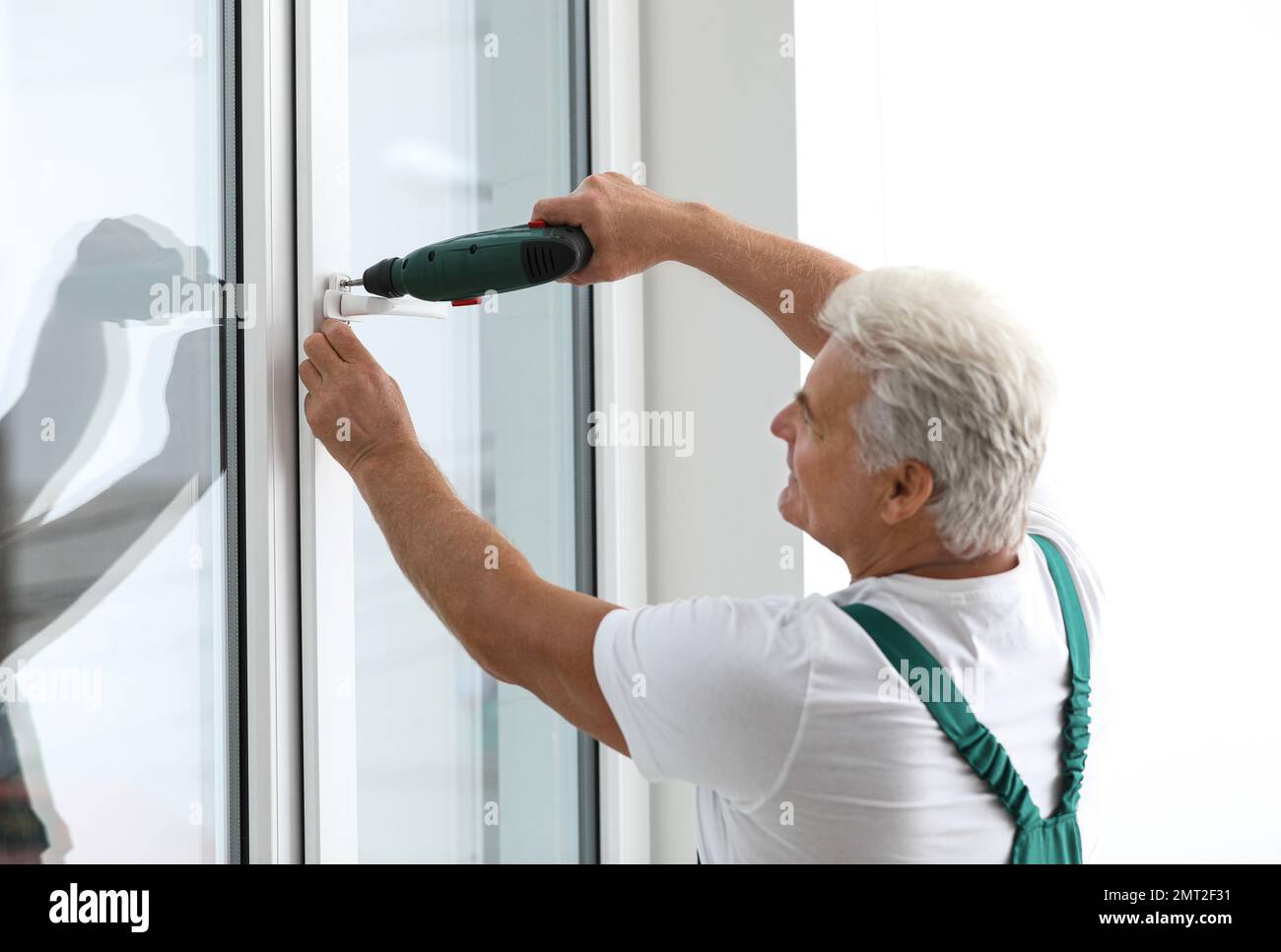 Mature construction worker repairing plastic window with electric ...
