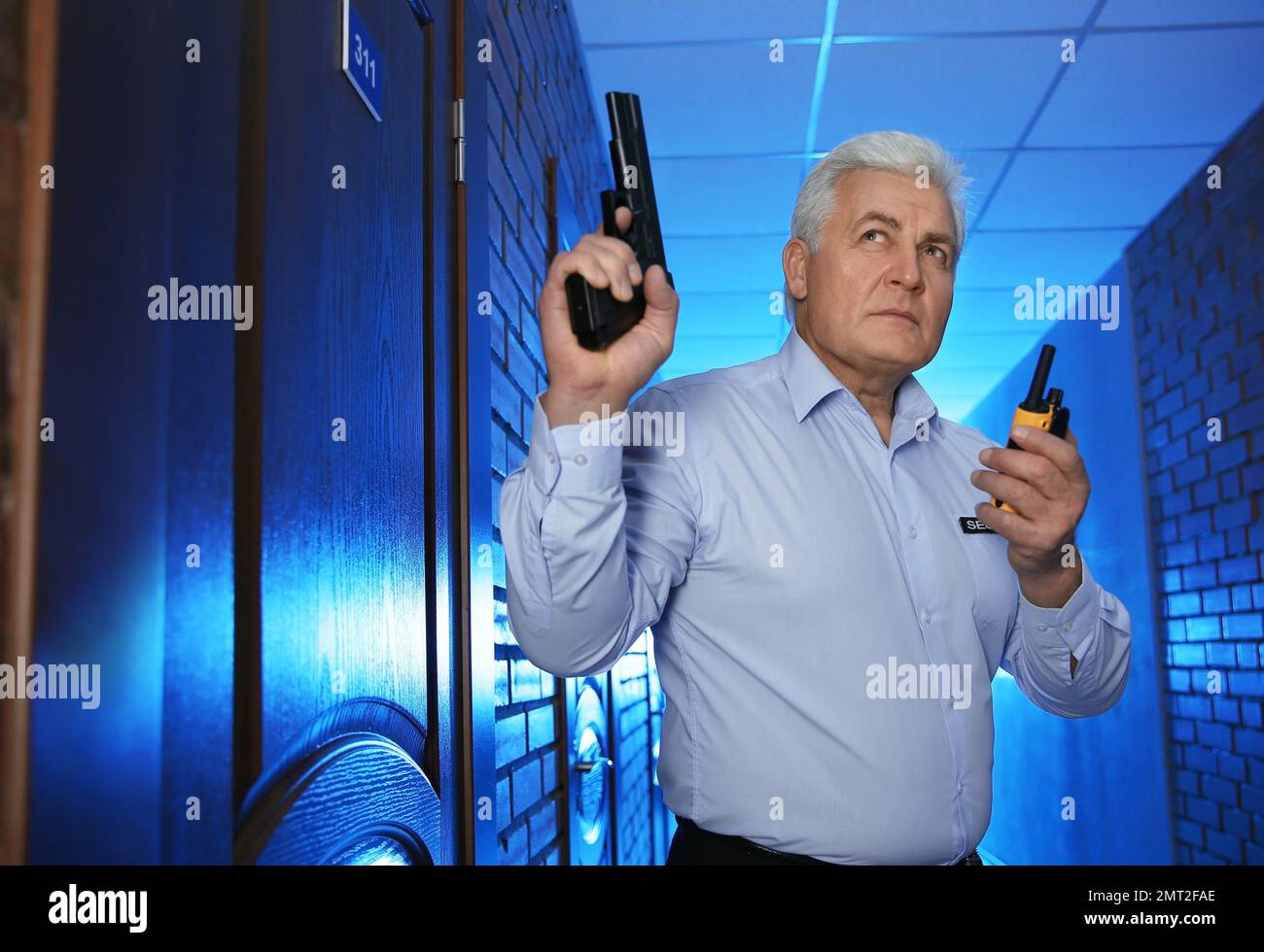 Professional security guard with gun and portable radio set in dark ...