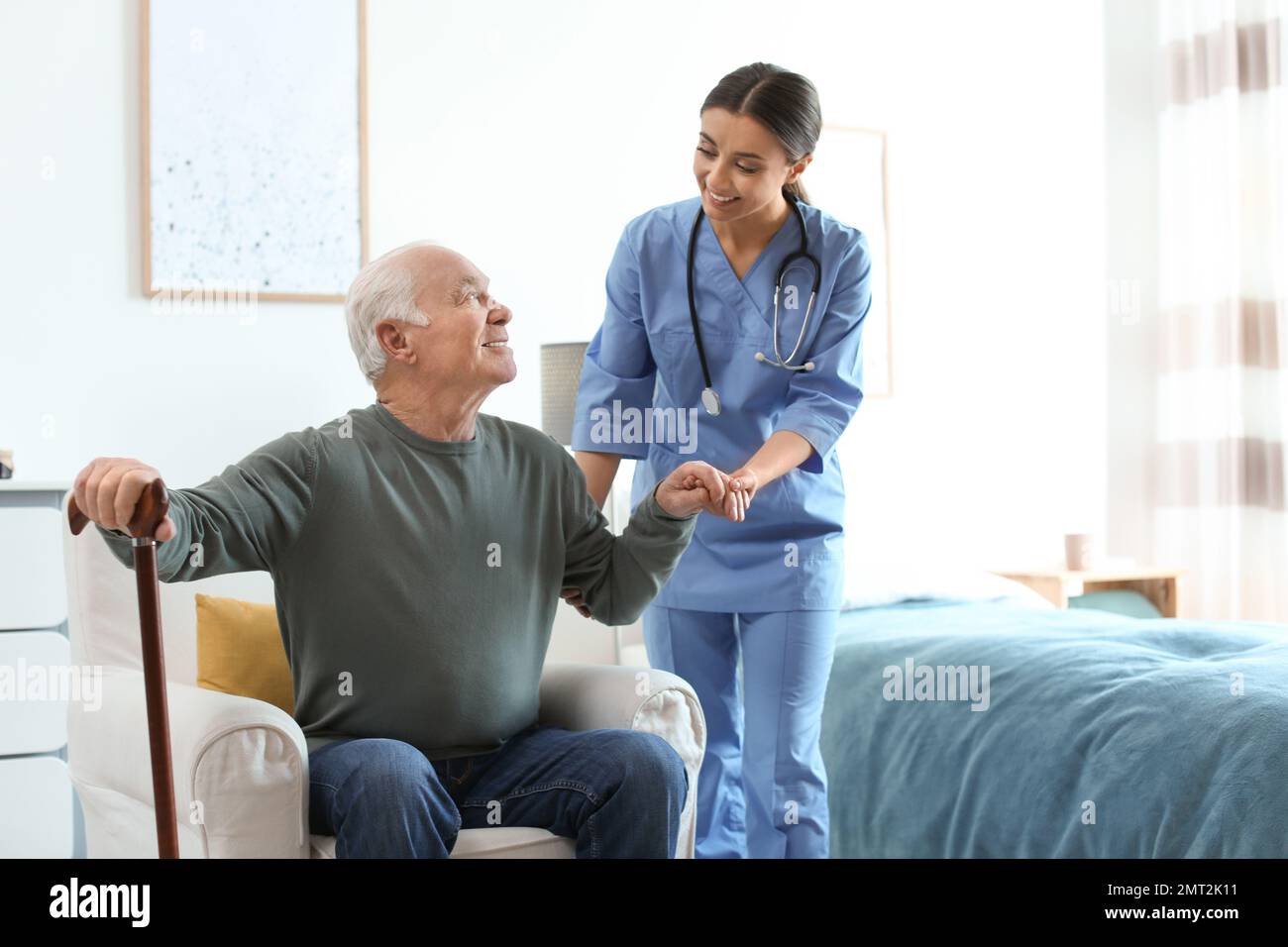 Care worker helping elderly man with stick in geriatric hospice Stock ...