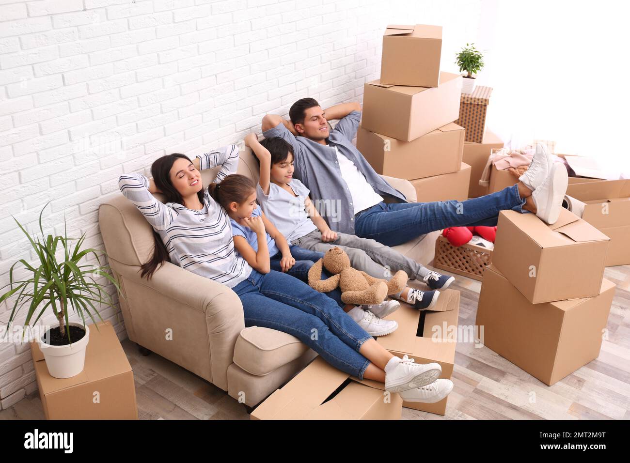 Happy family resting in room with cardboard boxes on moving day Stock ...