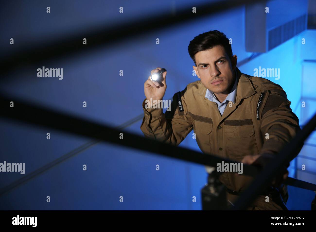 Professional security guard with flashlight on stairs in dark room ...