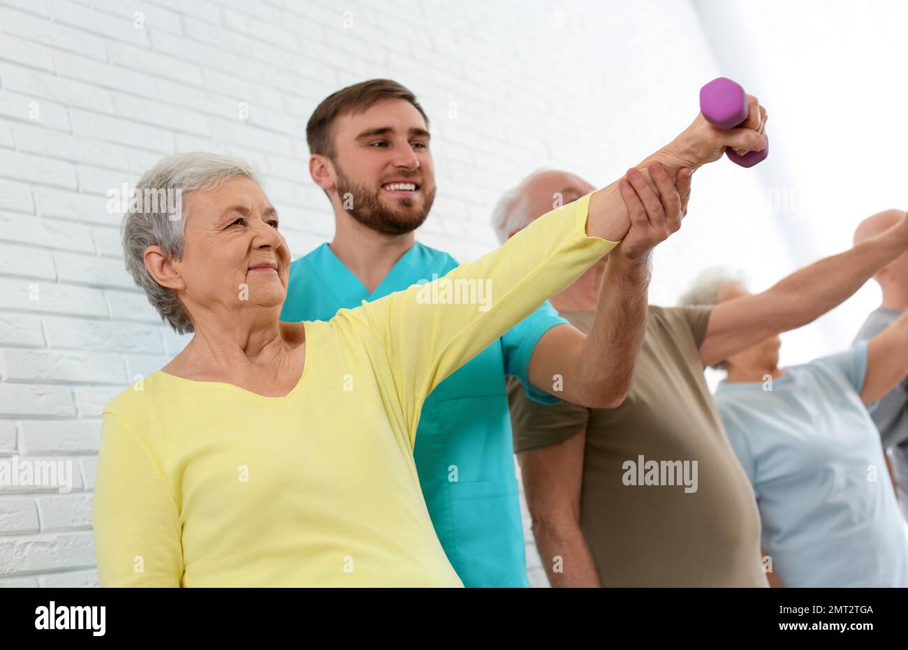 Care worker helping elderly woman to do exercise with dumbbell in ...
