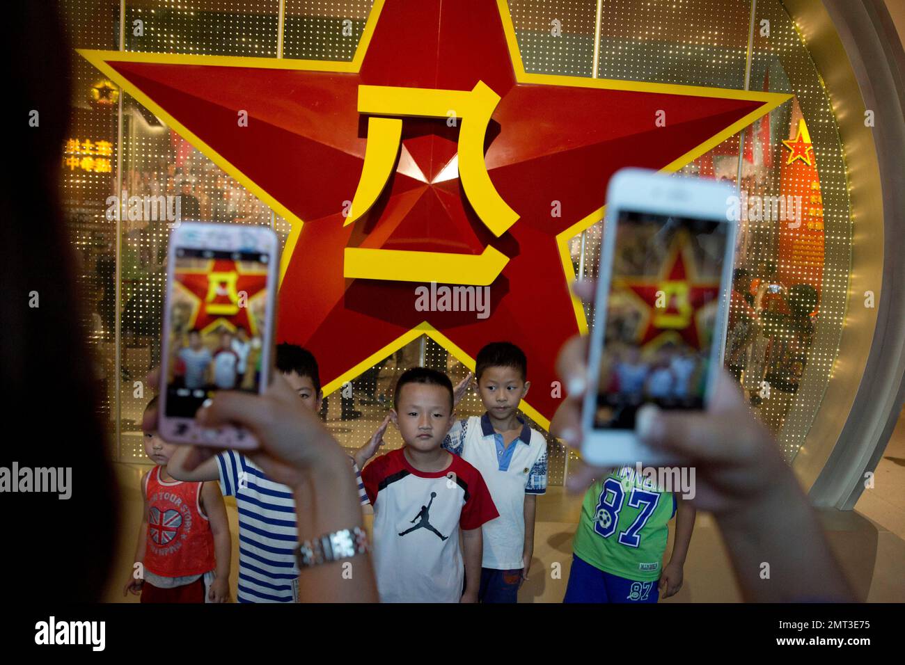 Chinese children salute as they pose for photos in front of the emblem ...