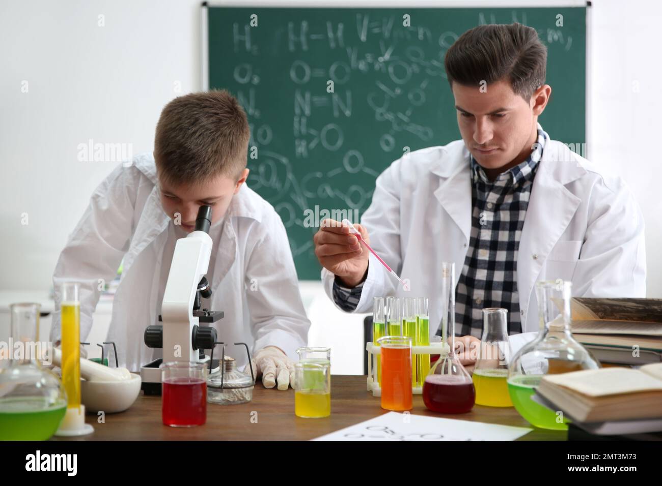 Teacher with pupil making experiment at table in chemistry class Stock ...