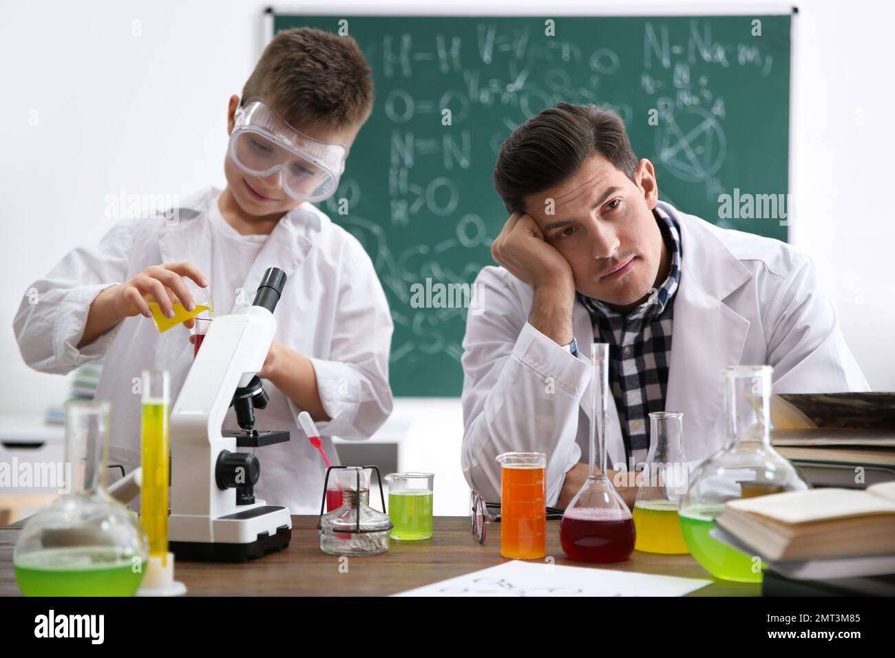 Teacher with pupil making experiment at table in chemistry class Stock ...