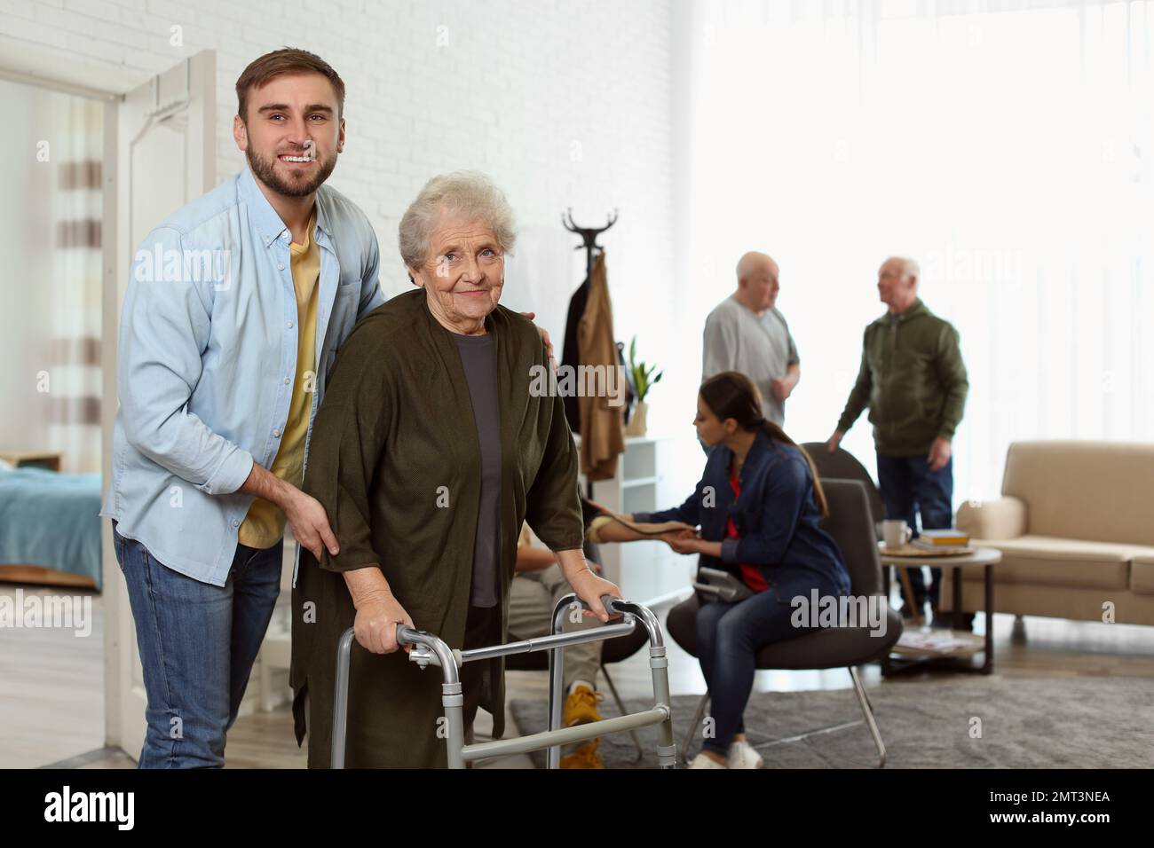 Care worker helping to elderly woman with walker in geriatric hospice ...