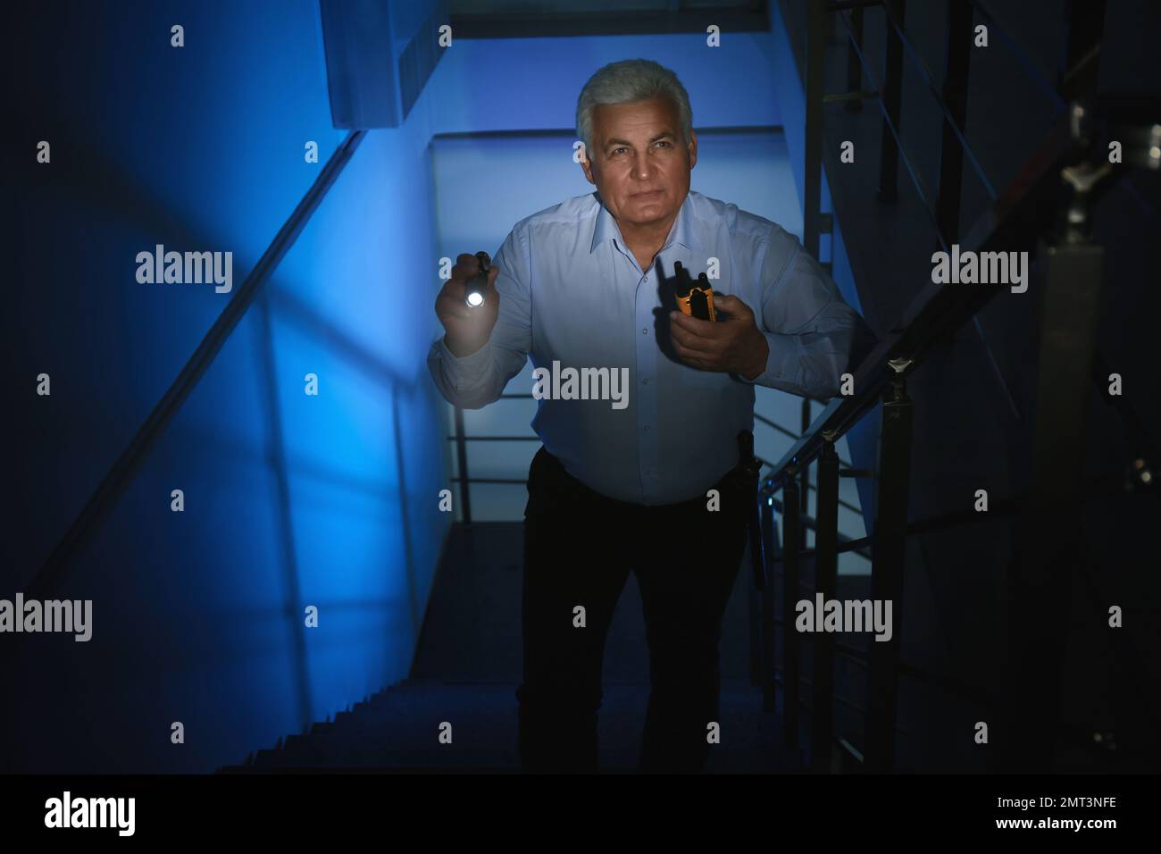Professional security guard with flashlight on stairs in dark room ...