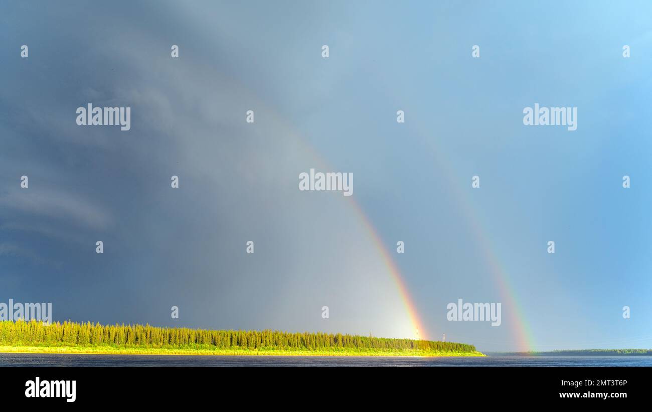 A double rainbow against a backdrop of bright blue clouds emerges from ...