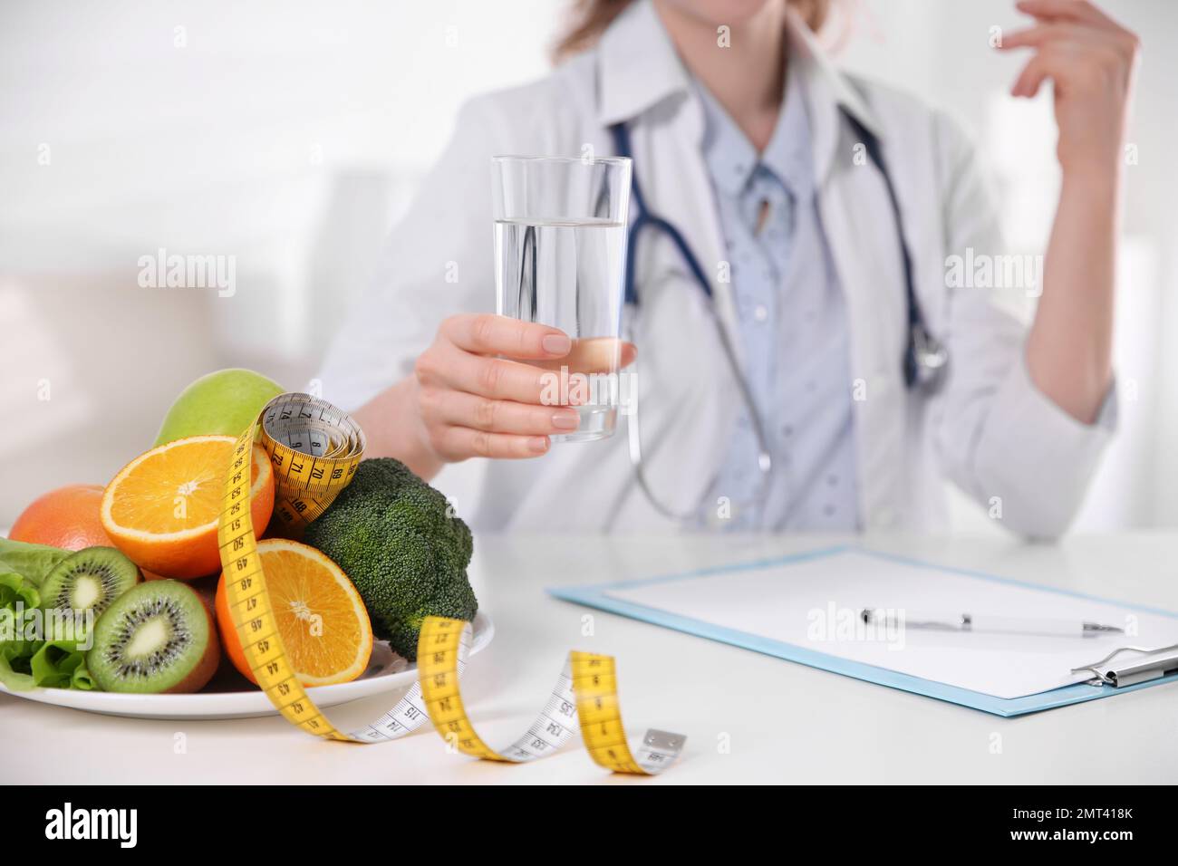 Nutritionist with glass of water, fruits, vegetables and measuring tape in office, closeup Stock ...