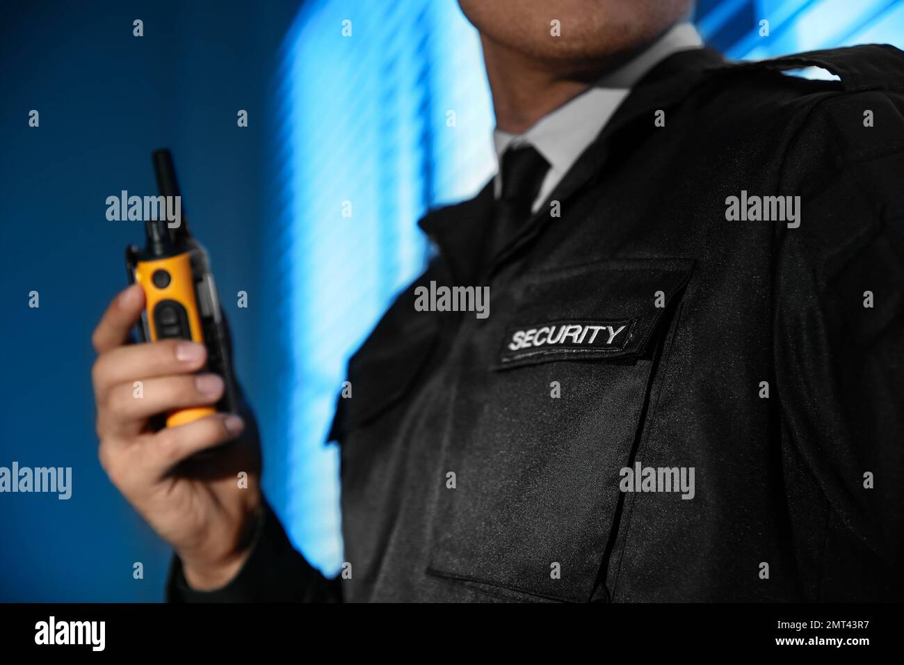 Professional security guard with portable radio set near window in dark ...