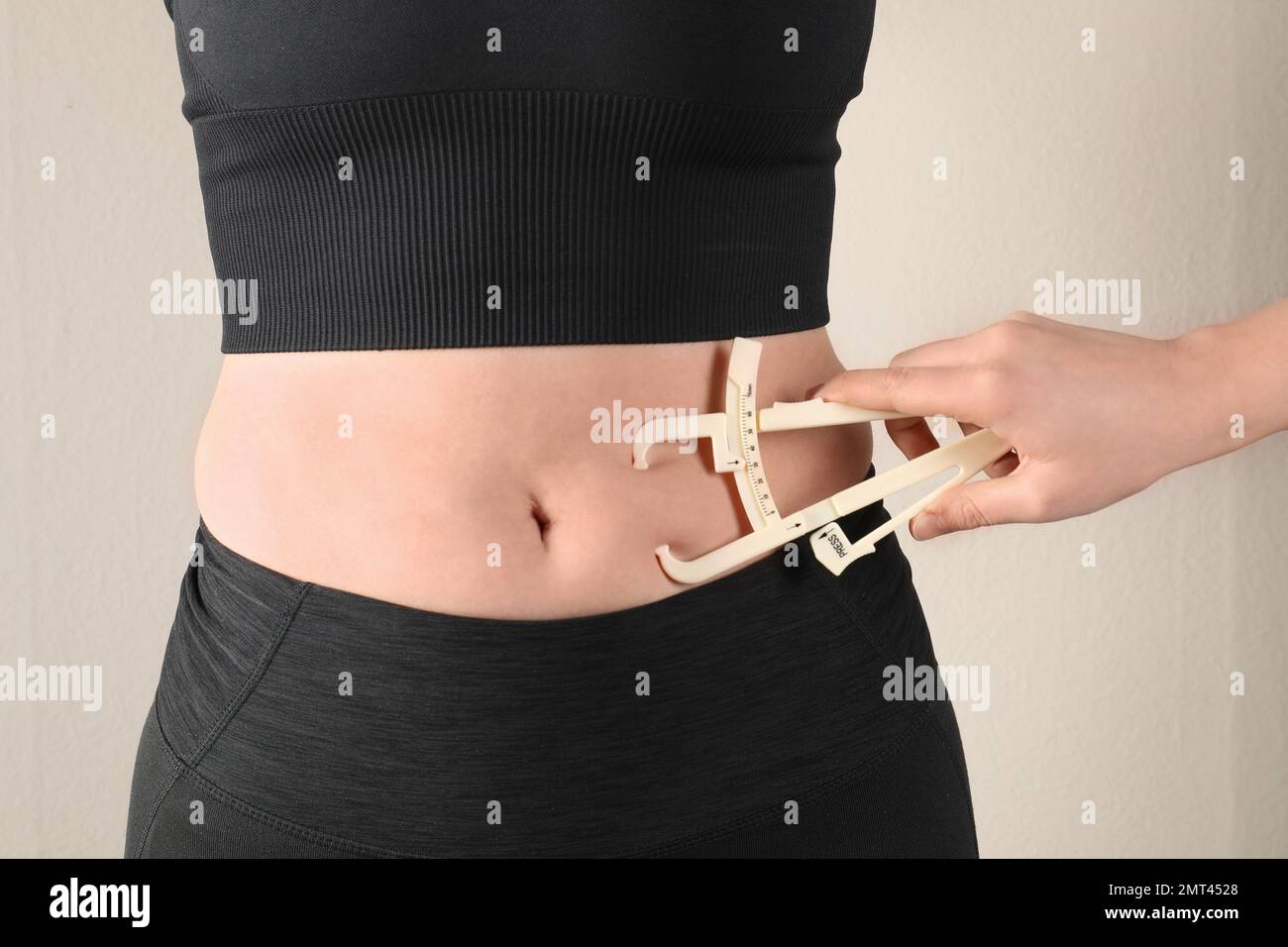 Nutritionist measuring woman's body fat layer with caliper on beige ...