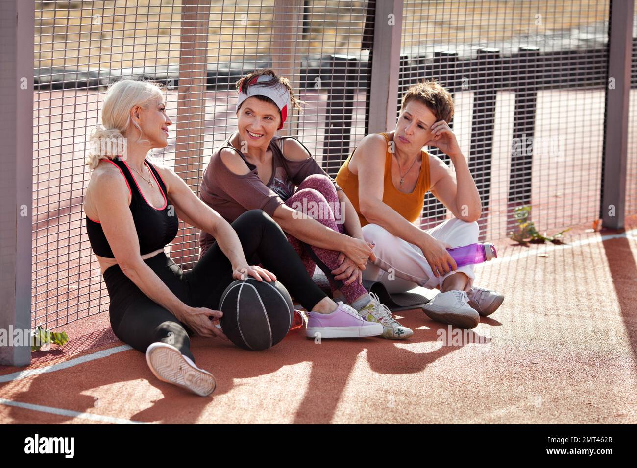 Happy mature women relax on court after playing basketball. Female aged ...