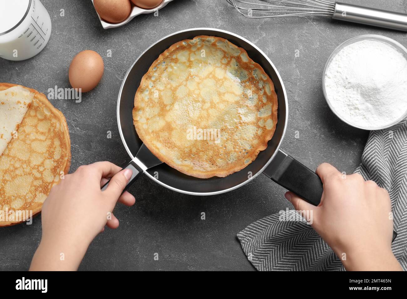Woman holding frying pan with thin pancake at grey table, top view ...