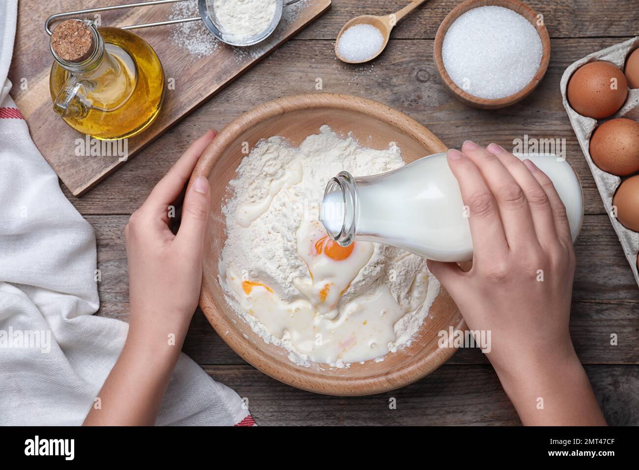 Woman preparing batter for thin pancakes at wooden table, top view ...