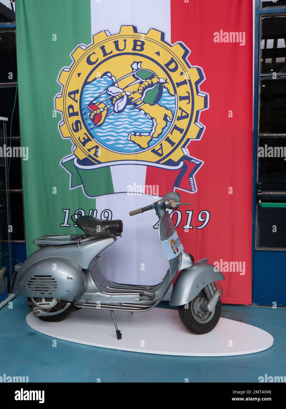 A Vespa scooter on display in front of the 'Vespa Club of Italy" flag ...