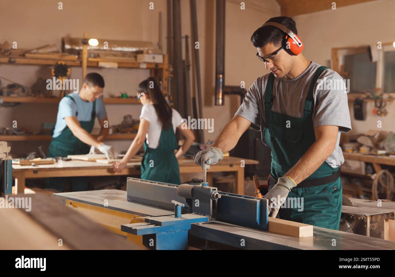 Professional carpenter working with surface planer and colleagues in ...