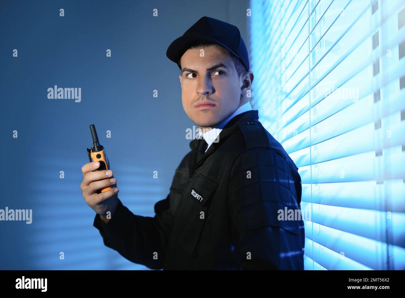 Professional security guard with portable radio set near window in dark ...