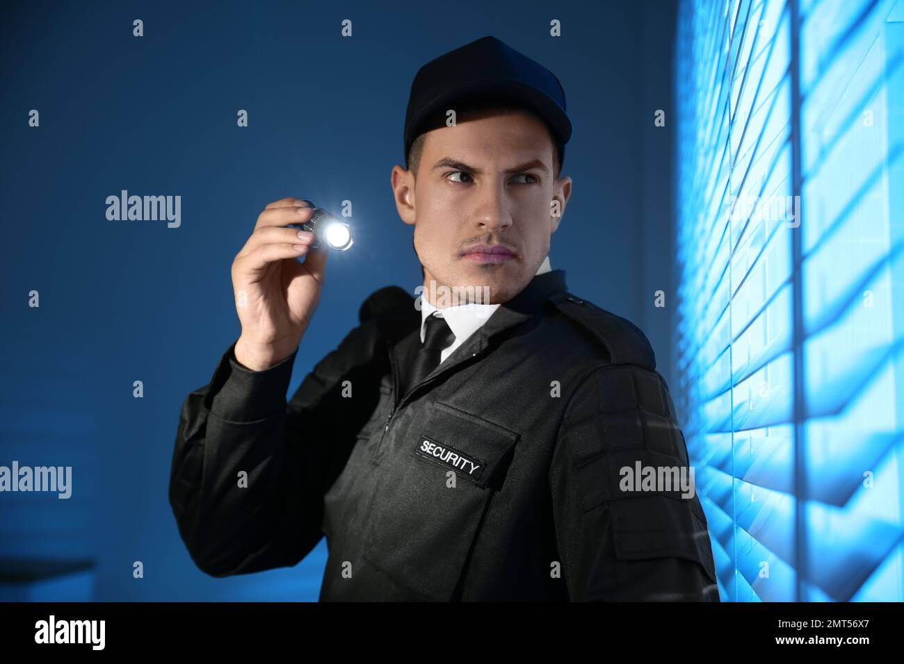 Professional security guard with flashlight near window in dark room ...