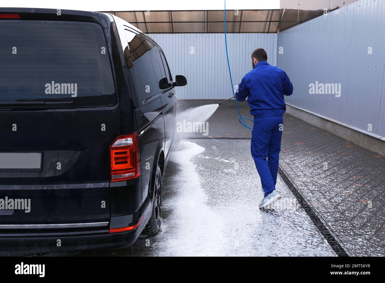Worker cleaning automobile with high pressure water jet at car wash ...